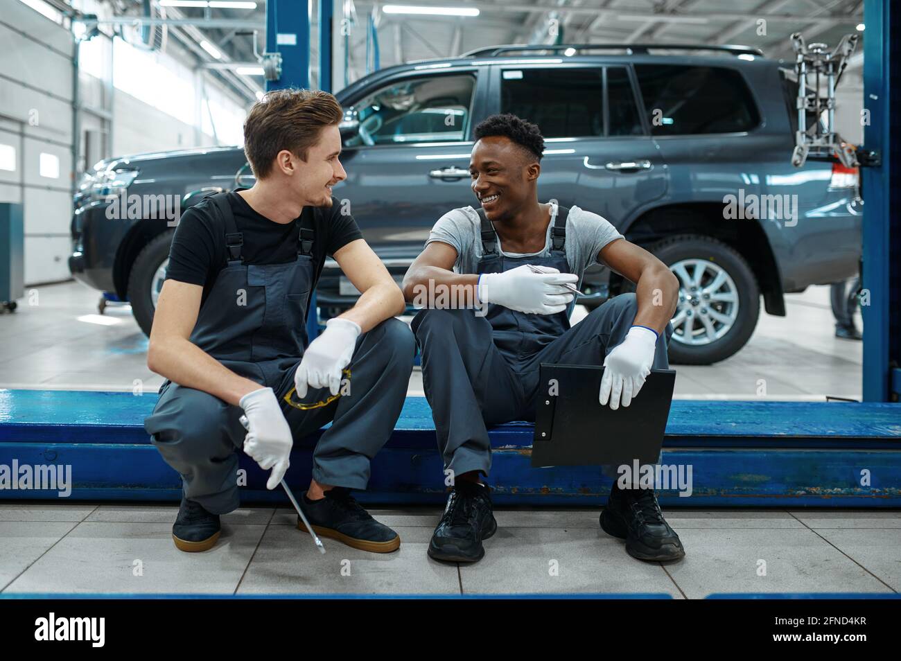 Two mechanics sitting on car lift in auto service Stock Photo - Alamy