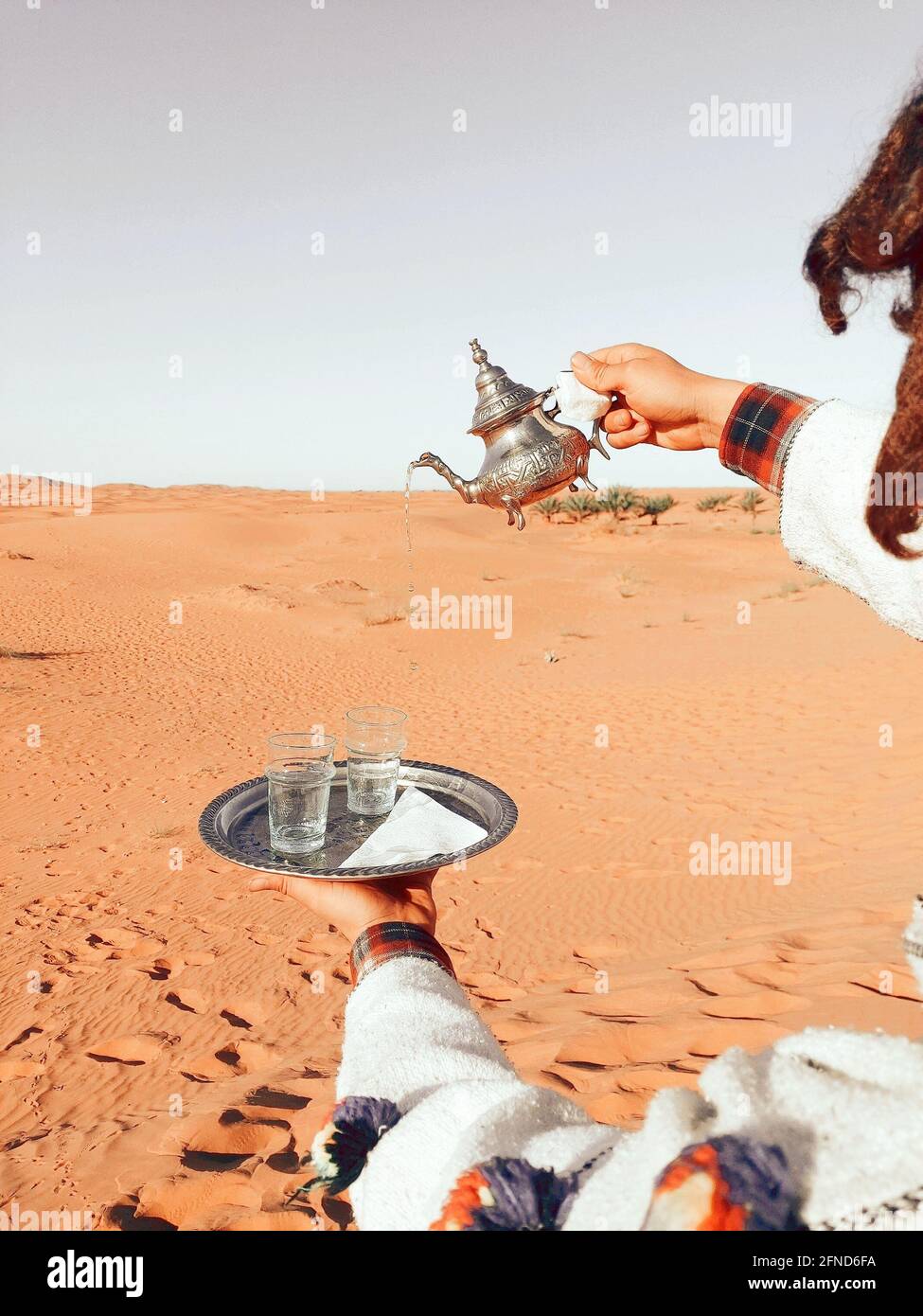 A hand pouring tea into a glass during Ramadan tea time in background ...
