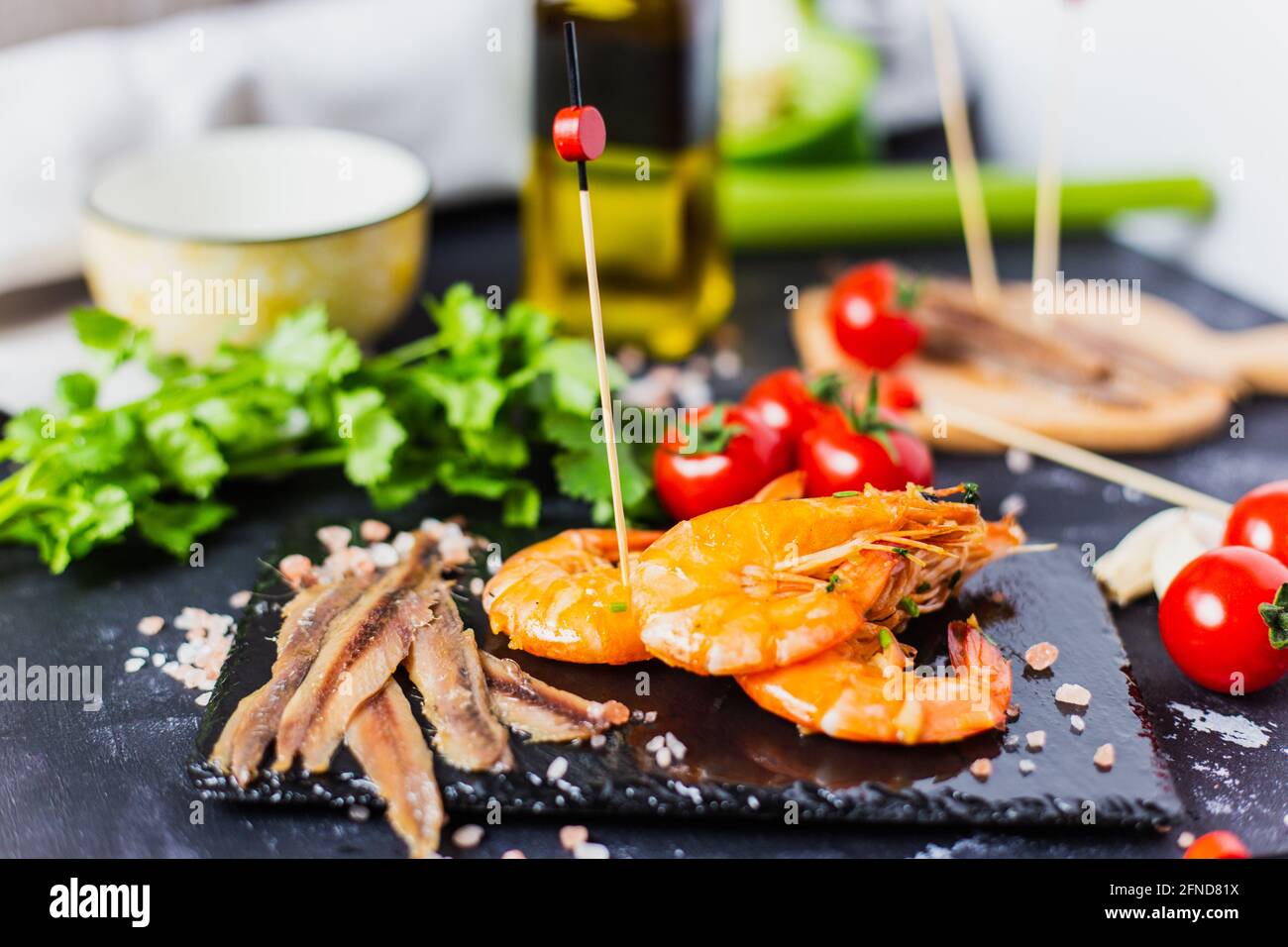Yummy anchovies and shrimps on a black platter; fresh greens, cherry ...