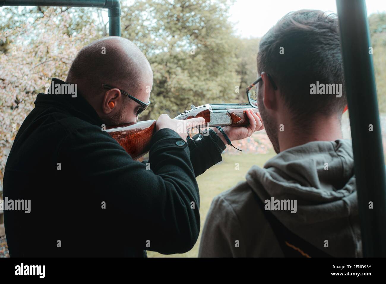 Two men practicing clay shooting. One teaching the other newbie the ...