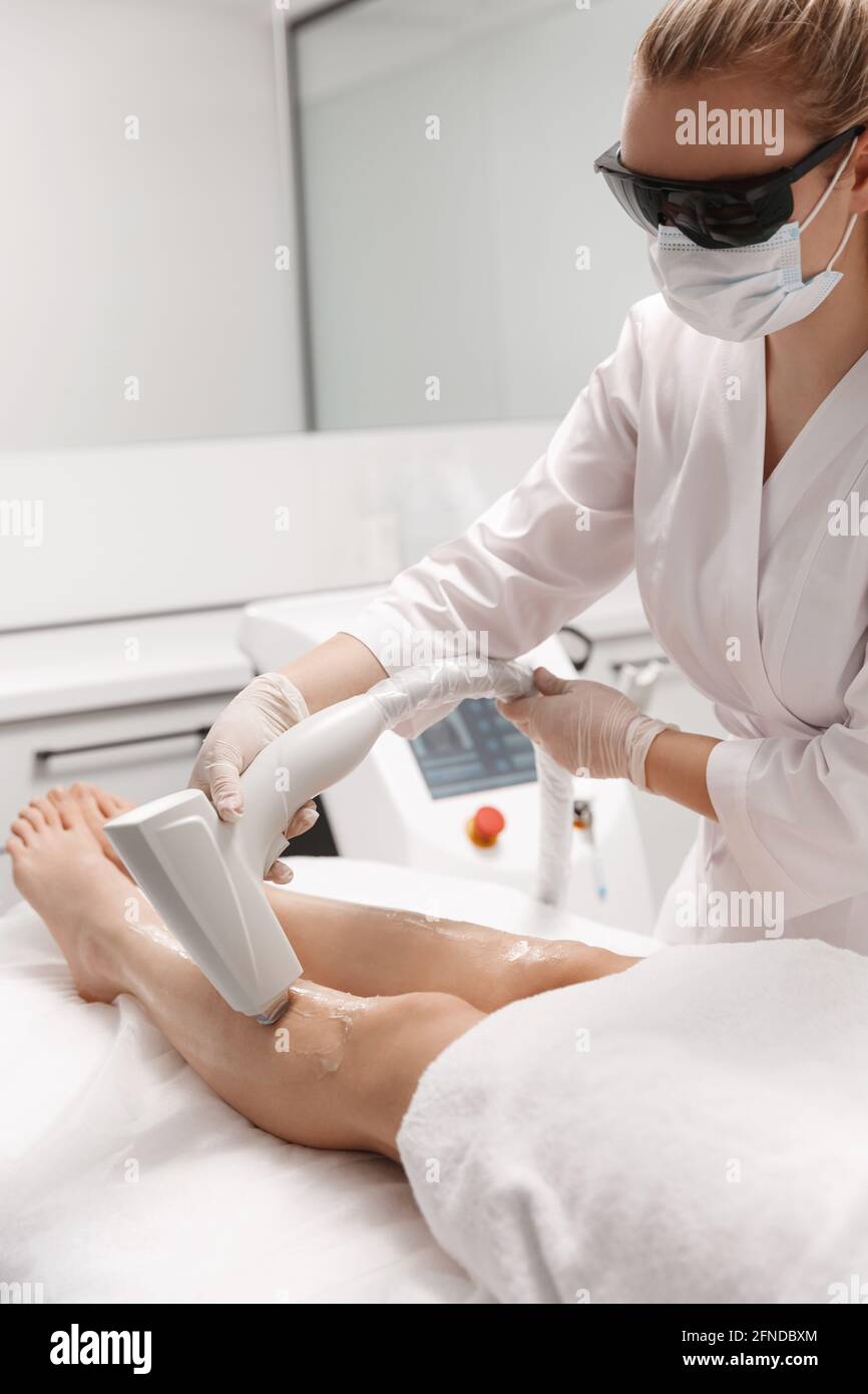 Vertical shot of beautician depilation master using laser for legs hair ...