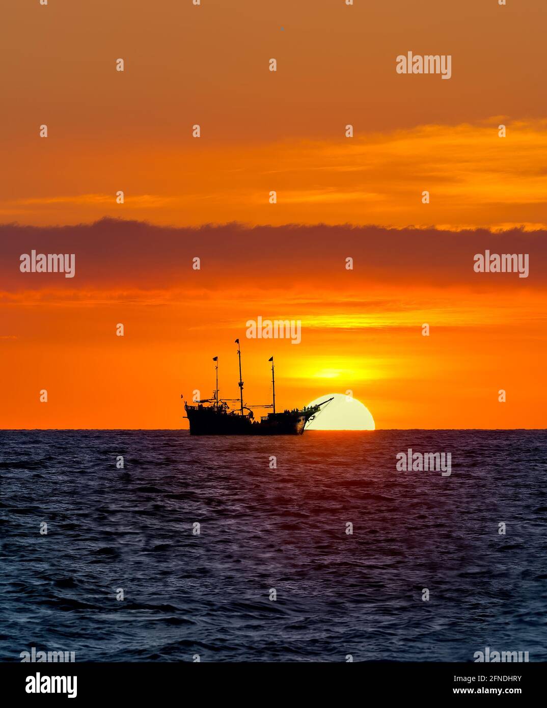 A Pirate Ship Sits On The Ocean Silhouetted Against A Colorful Orange ...