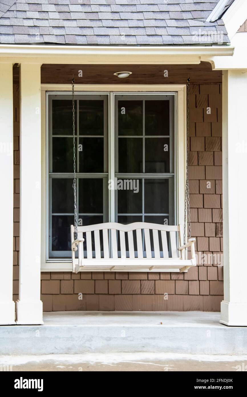 White porch swing in front of window and between columns of a brown ...