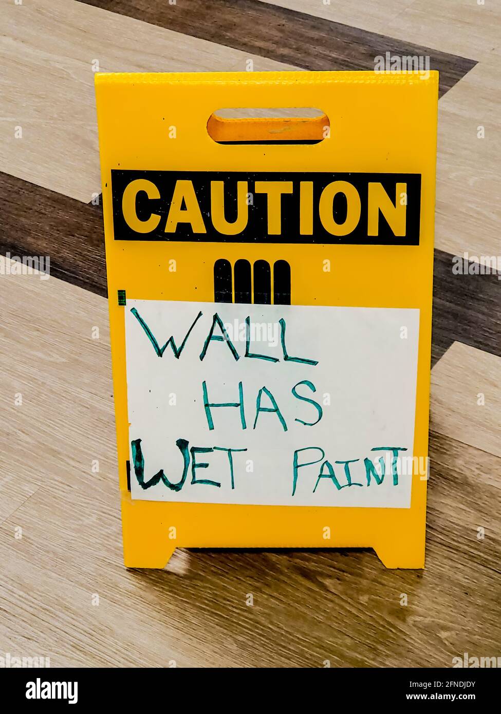 Yellow standing Caution sign sitting on parquet wood floor with white ...