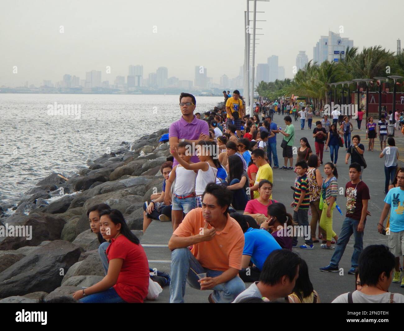 Filipino visitors walk and sit near the waterfront behind Mall of Asia ...