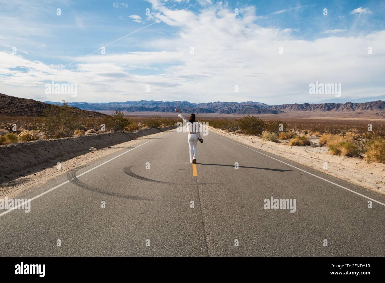 A young woman dressed in white running down a desolate road in the ...