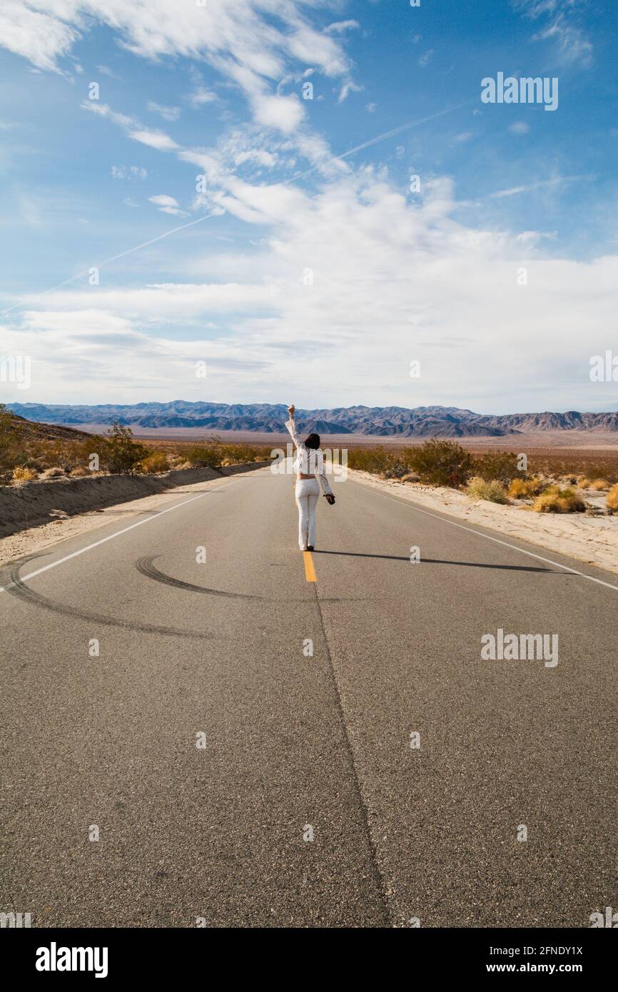 A young woman dressed in white running down a desolate road in the ...