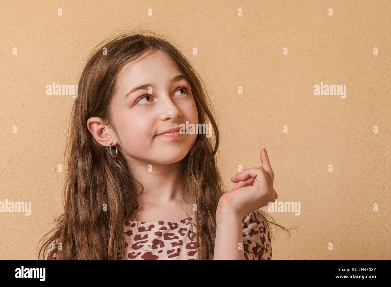 Teenage girl looks to the side with surprise on beige background ...