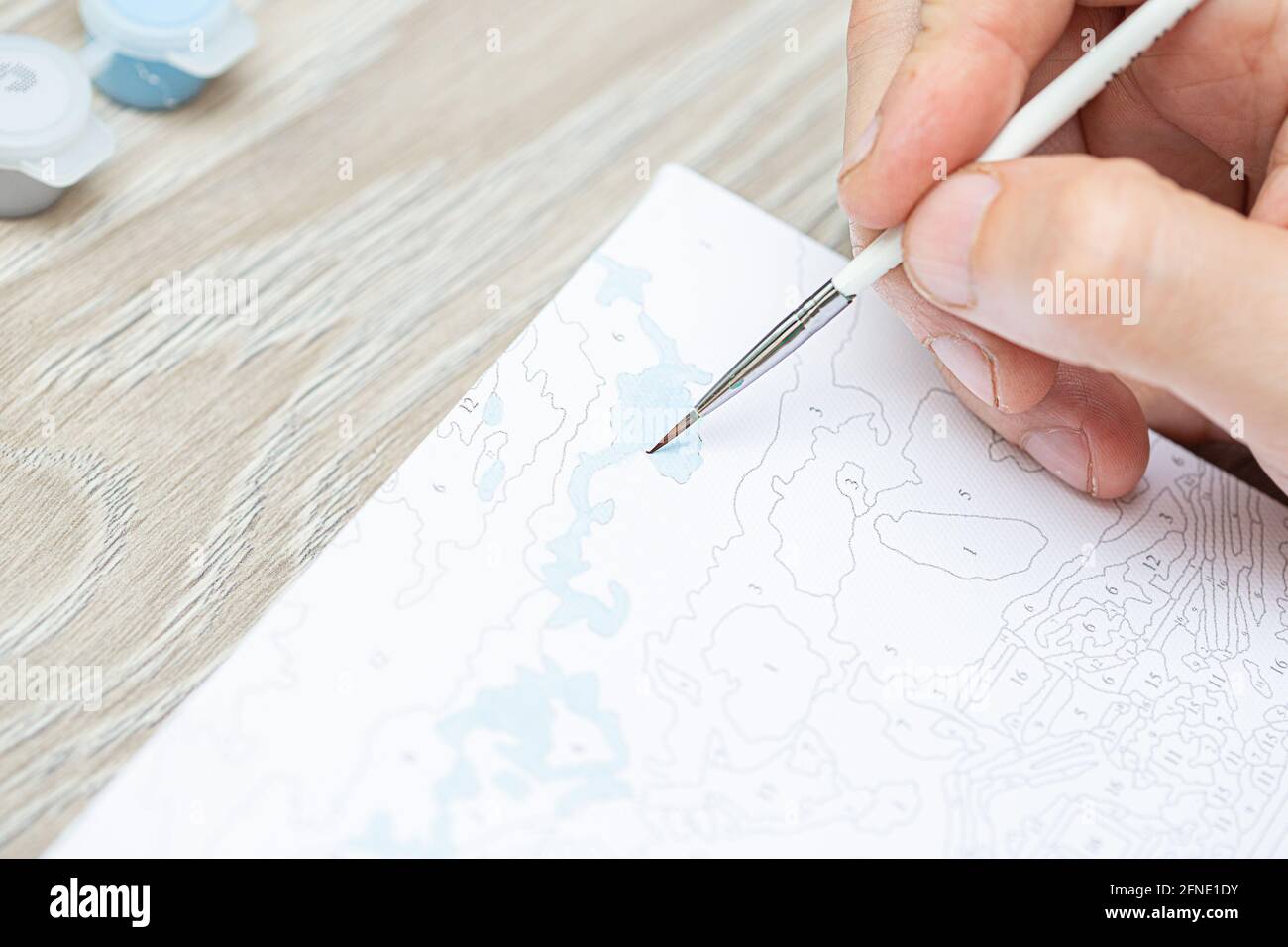 A mans hand holds a brush and draws a picture by numbers. Drawing on ...
