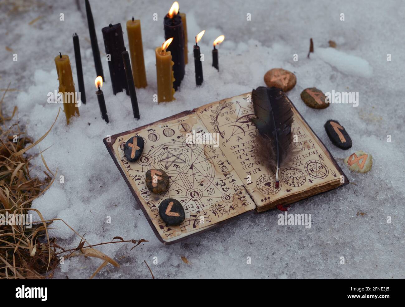 Open with book of magic spells, runes on stones and candles in snow ...
