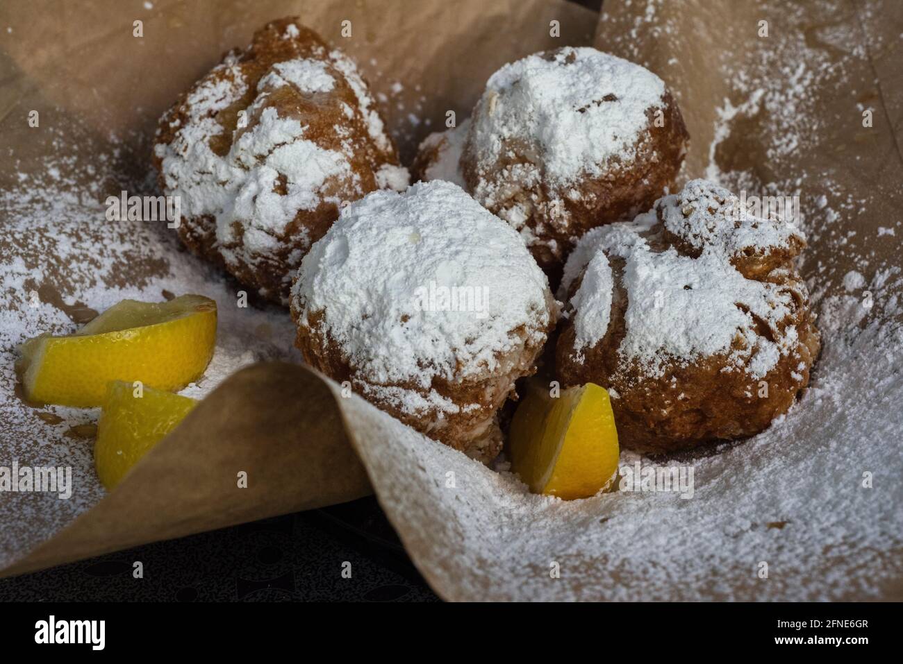 Four beignets are served on brown paper with lemon slices and covered ...
