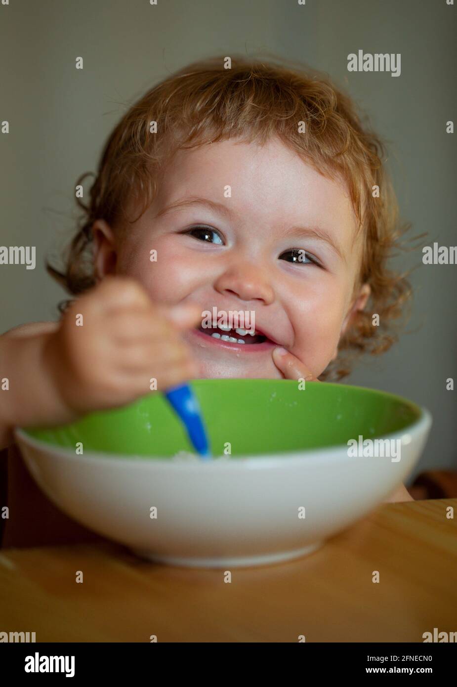 Baby holding a spoon in his mouth. Happy child eating himself with a ...
