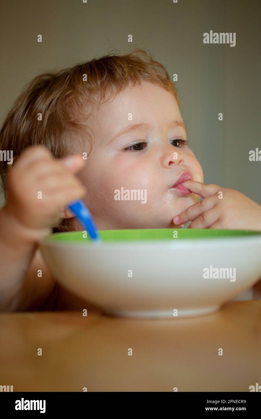 Funny little baby in the kitchen eating with fingers from plate. Lick ...