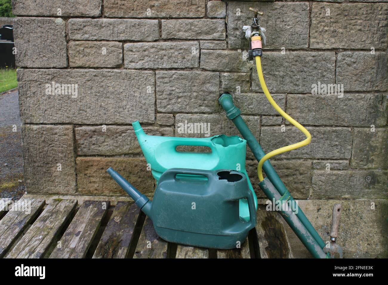 External water tap and two green watering cans on a slatted garden ...