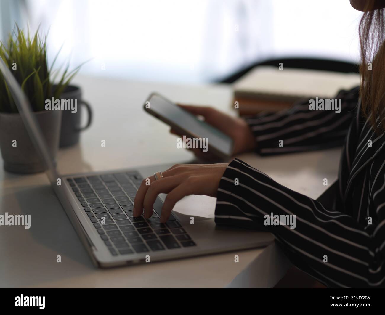 Side view of female hand typing on laptop and using smartphone on ...