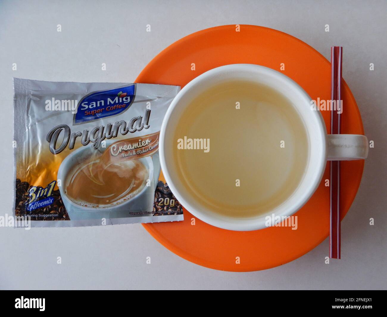 San Mig instant coffee close to a cup of hot water on an orange plate ...