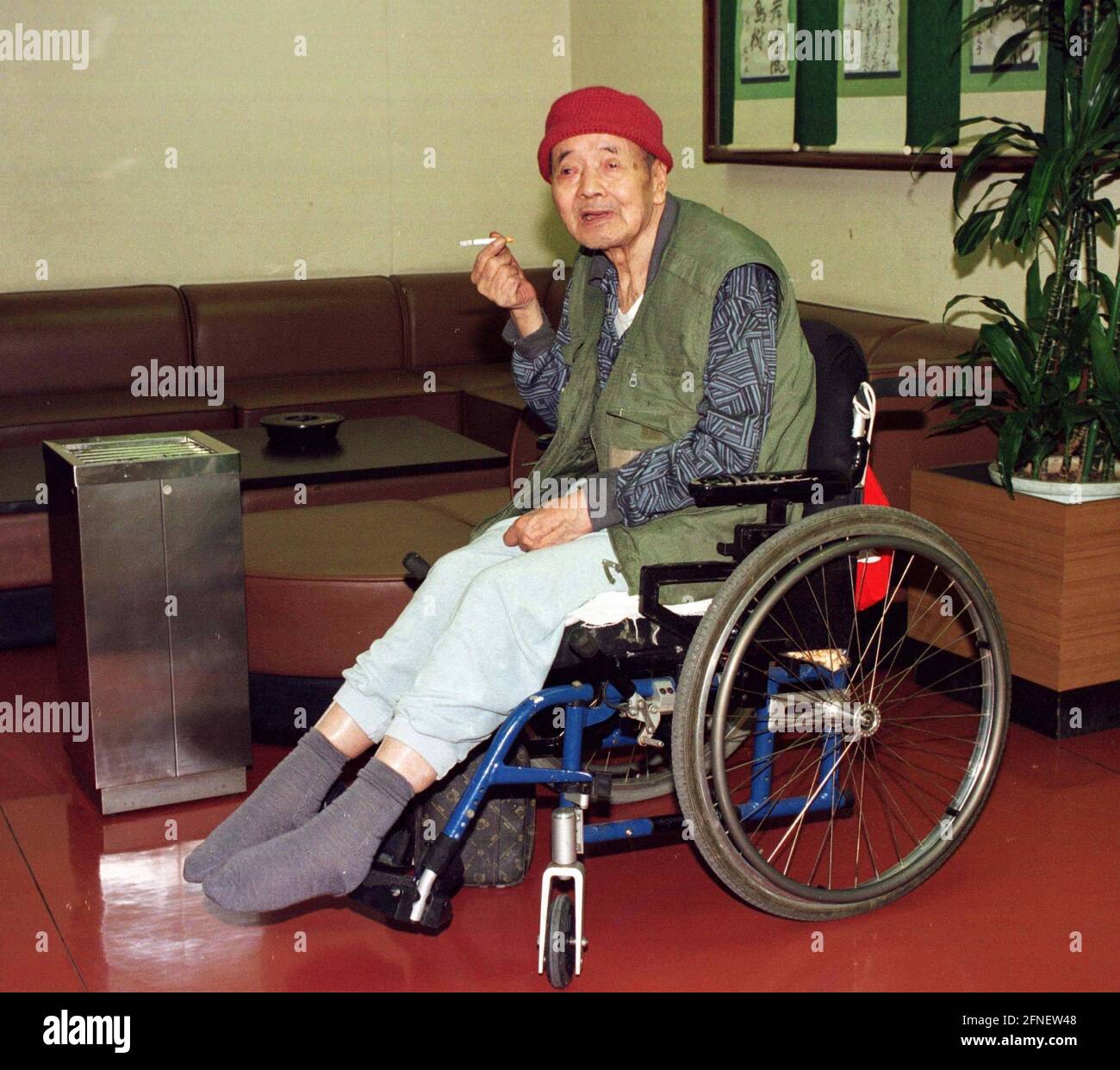 An old Japanese man in a wheelchair in the hallway of a retirement home ...