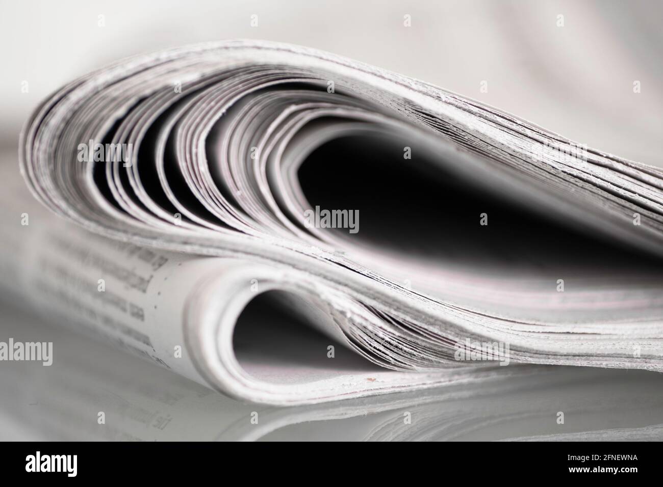 Two folded newspapers mirrored on glass table against plain background ...