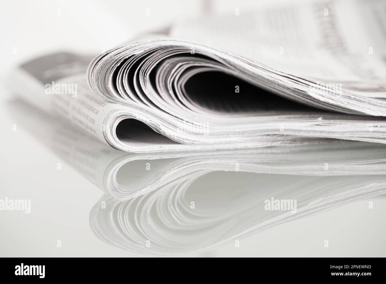 Folded newspaper mirrored on glass table against plain background with ...