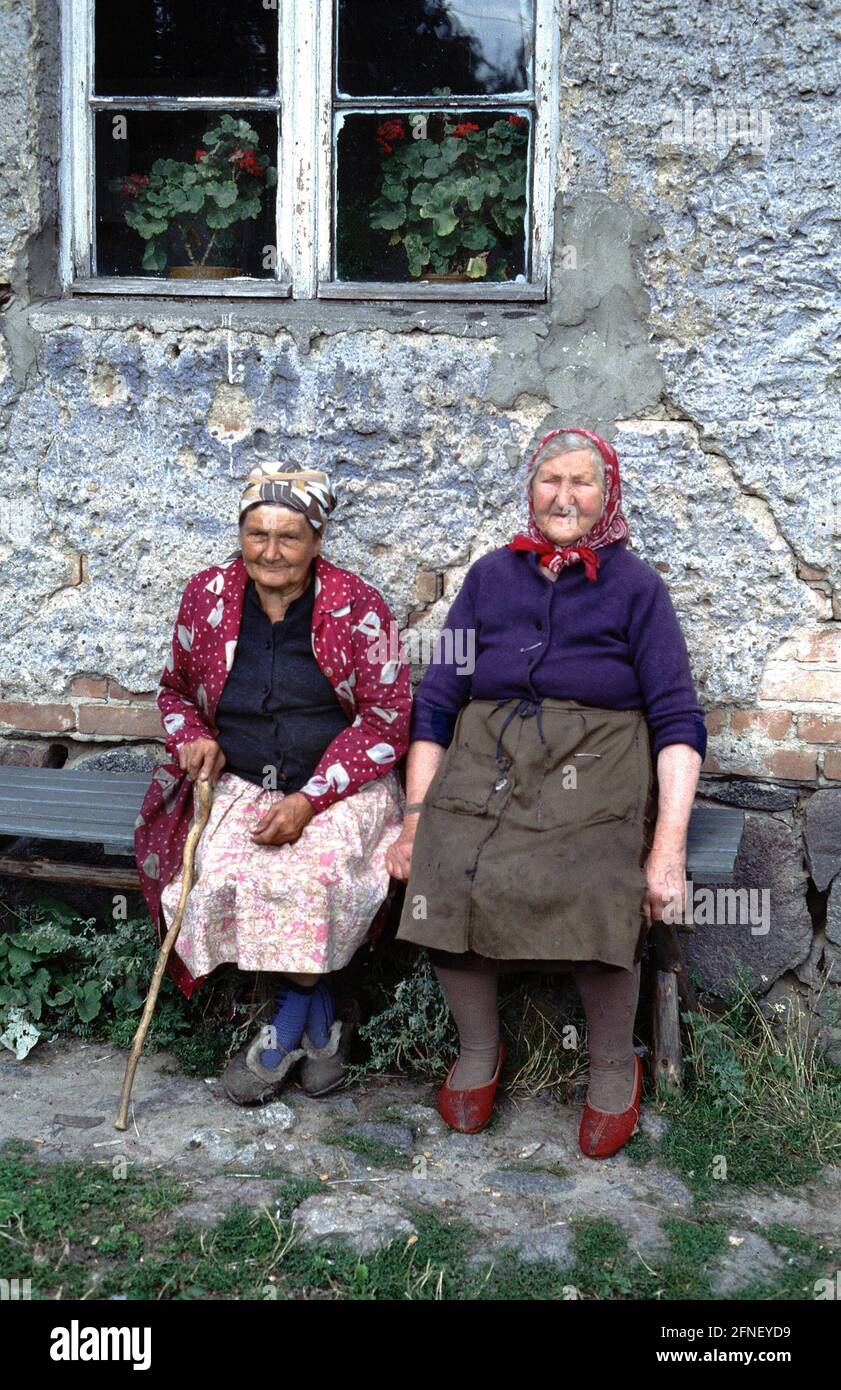 Two old peasant women on a bench in front of a house in a small village ...