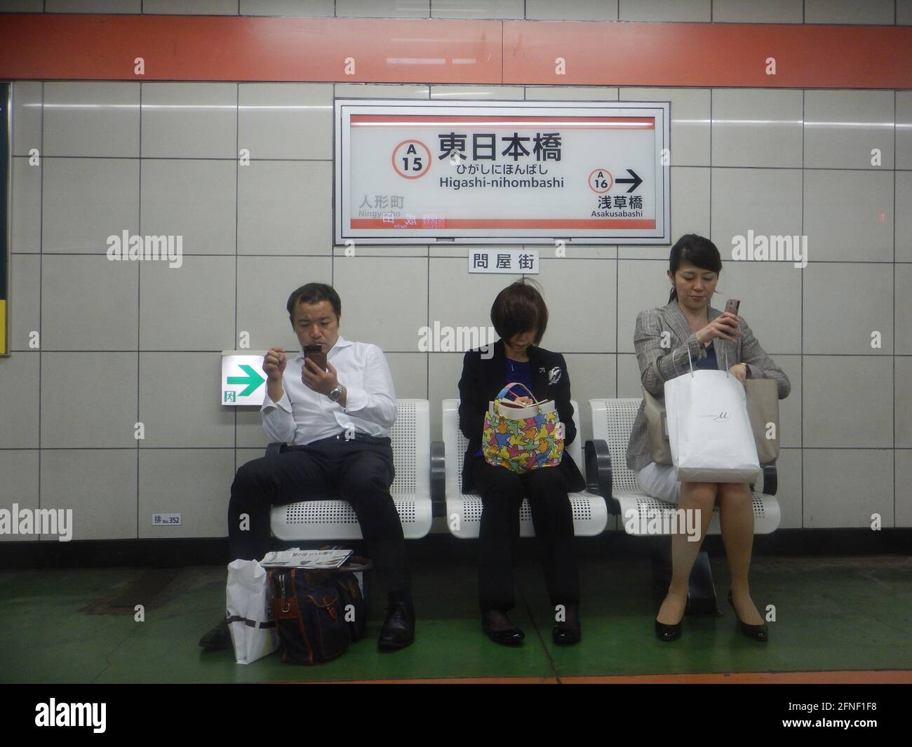 Three people waiting in the Japanese Higashi-nihombashi Metro station ...