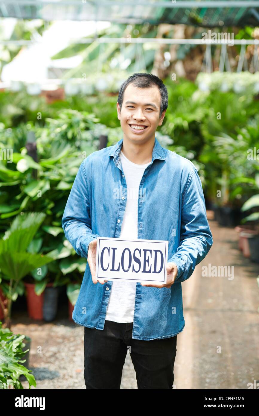 Cheerful young man holding closed sign when standing in gardening ...
