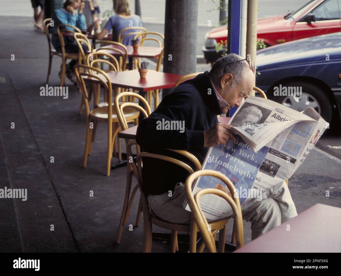 A man is reading the newspaper in a sidewalk cafe. [automated ...