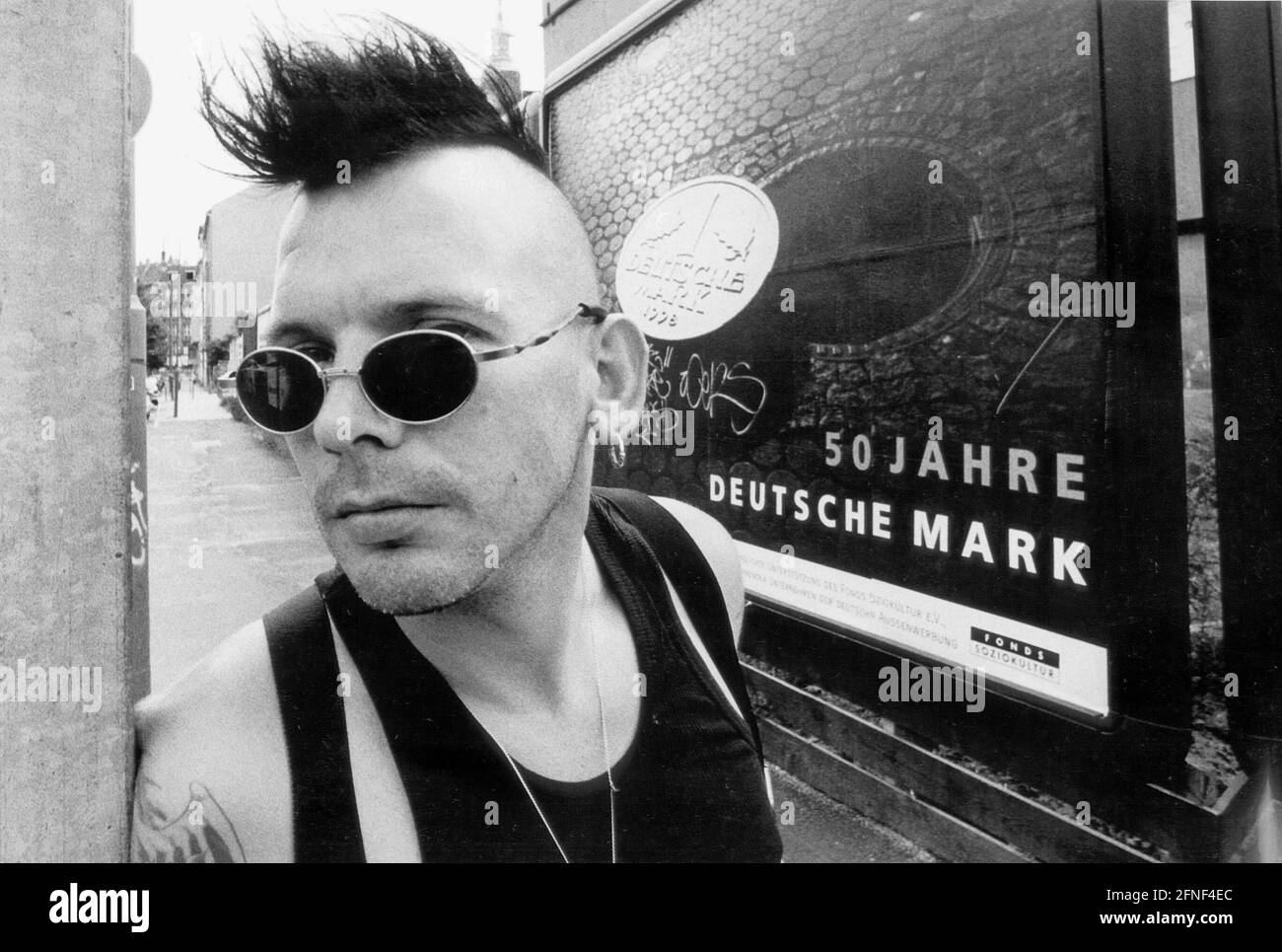 A punk in Berlin in front of a poster for '50 years of the German Mark ...