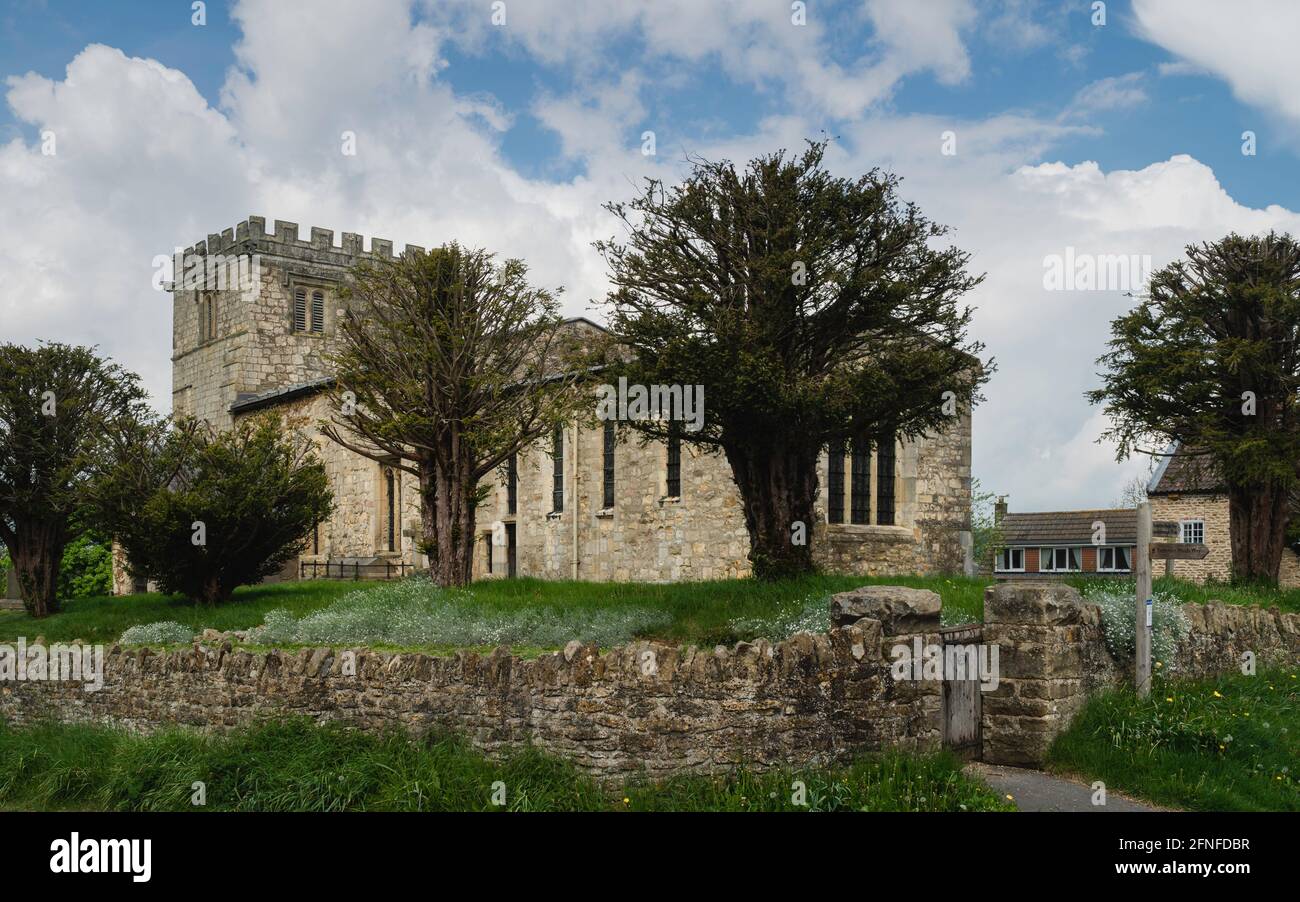 Ancient All Saints Church flanked by dry stone walling and trees with ...