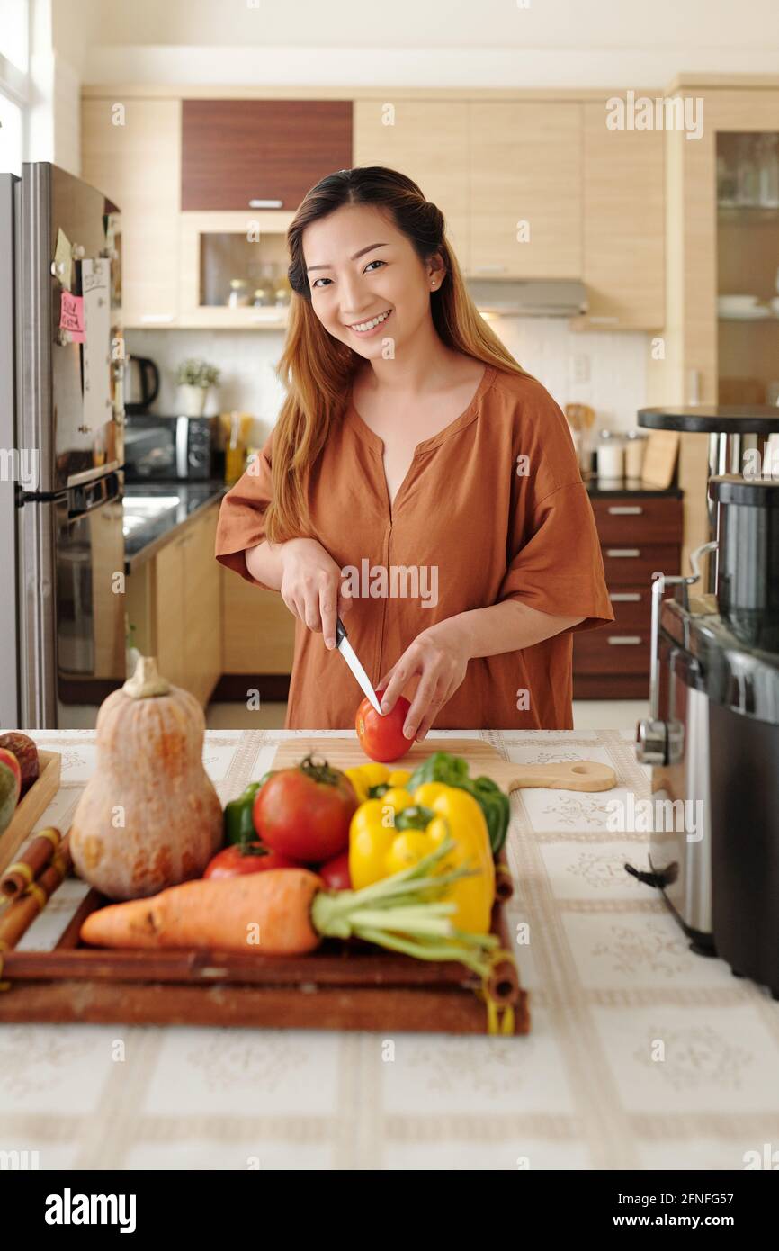Portrait of smiling pretty young woman enjoying cooking, she is cutting ...