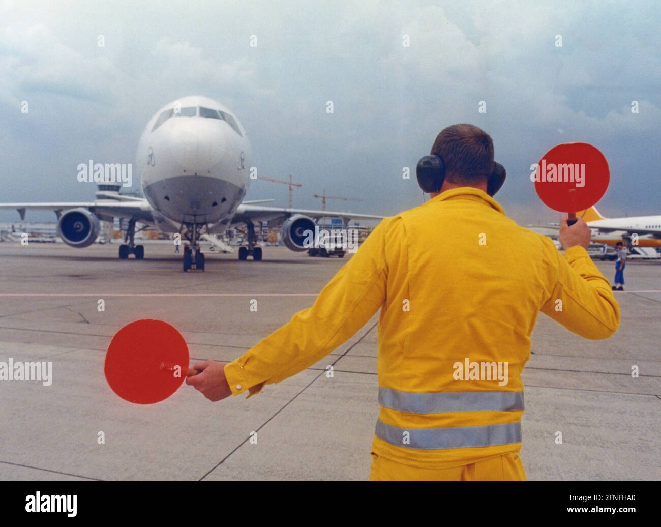 A ground controller waves in a landed aircraft on the apron of ...