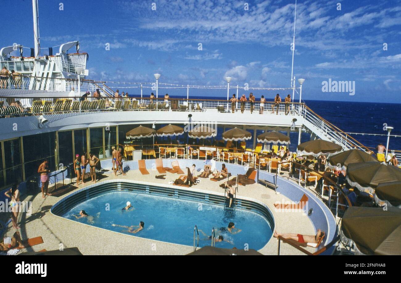 On the deck of a cruise ship, vacationers sunbathe by the pool ...
