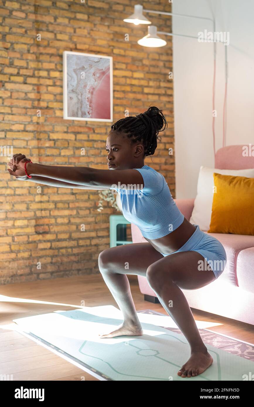Side view of fit black athlete doing squats while standing on mat and ...