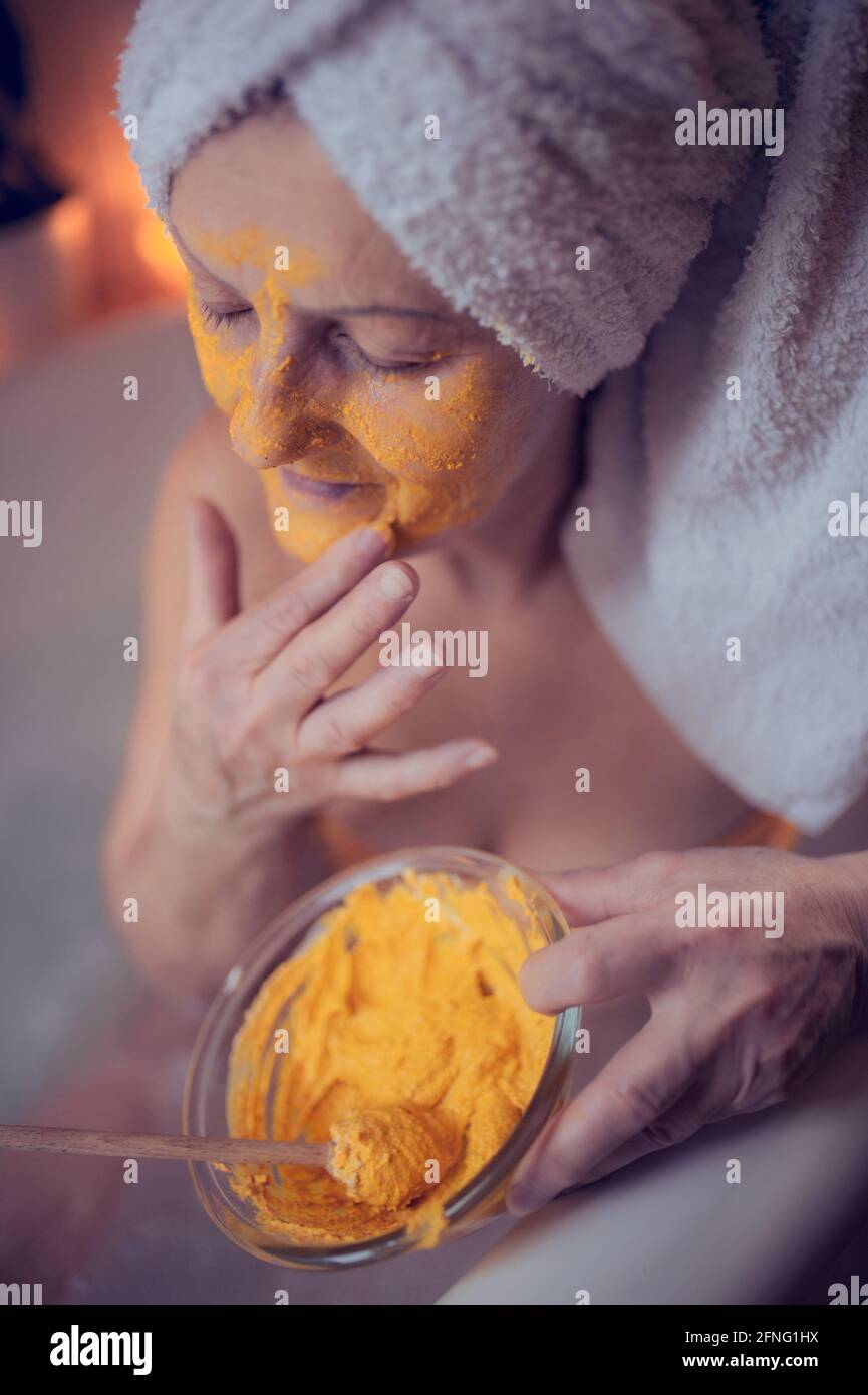 Happy senior woman applying beauty face mask in bath tub at home ...