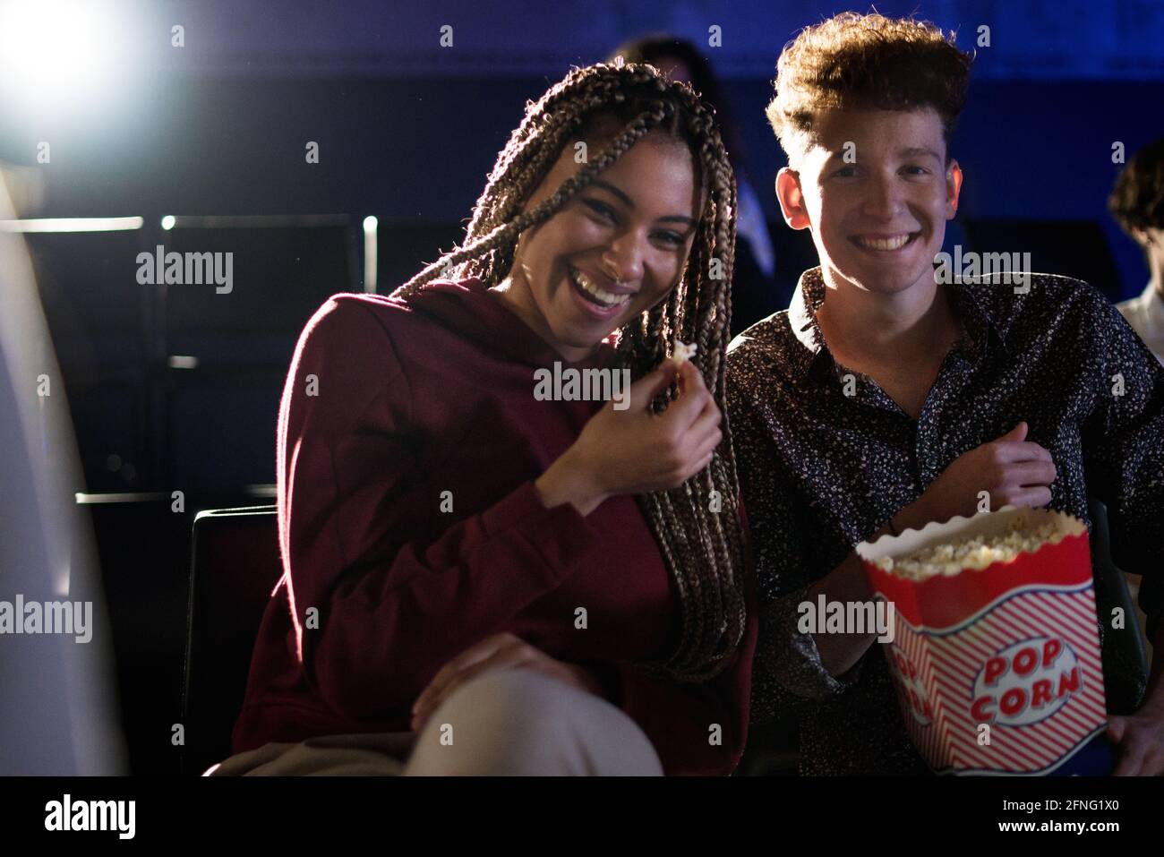 Young couple eating popcorn while watching movie in cinema, laughing ...