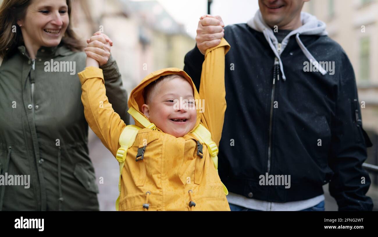 Happy family with down syndrome son outdoors on a walk in rain, having ...