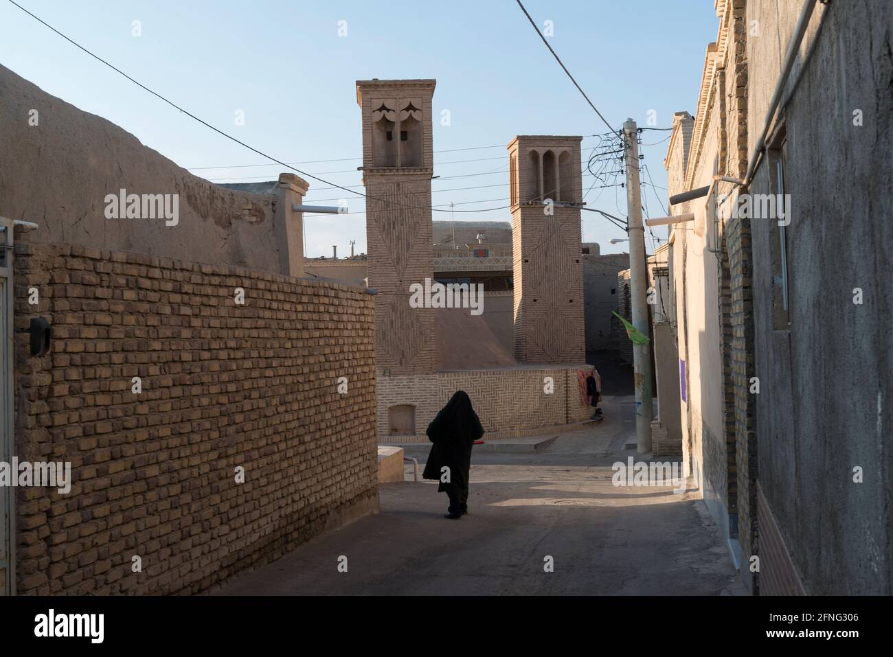 Woman in black chador walking in a street with an ab-anbar, an ...