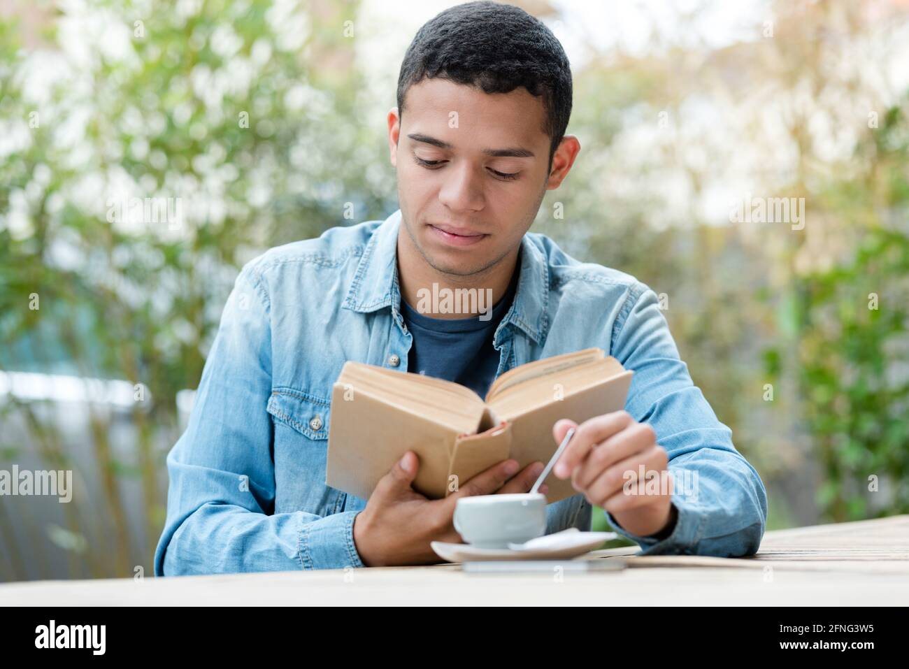 handsome young man drinking coffee while reading book Stock Photo - Alamy