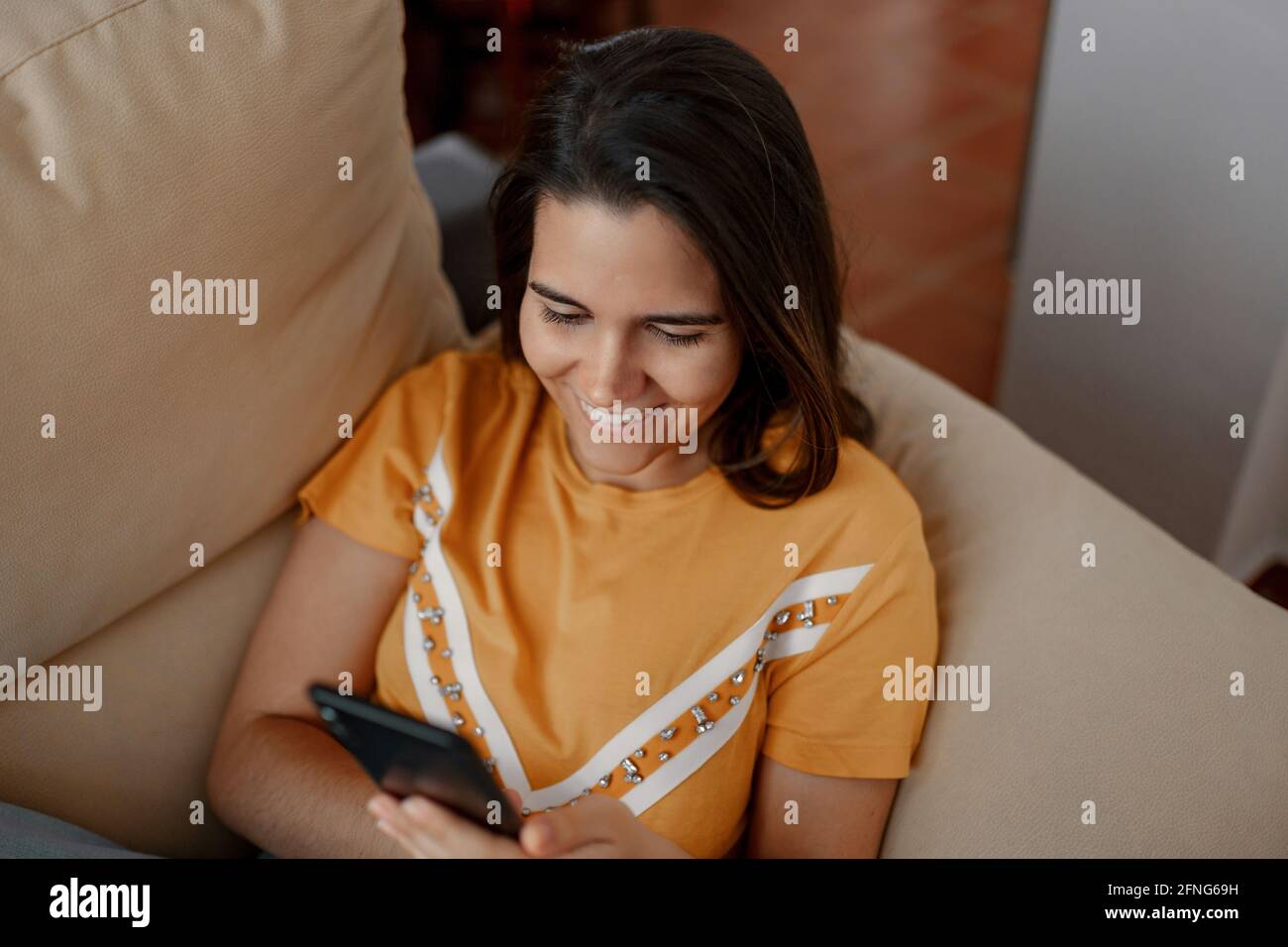 Young female text messaging on cellphone while lying down on couch in ...