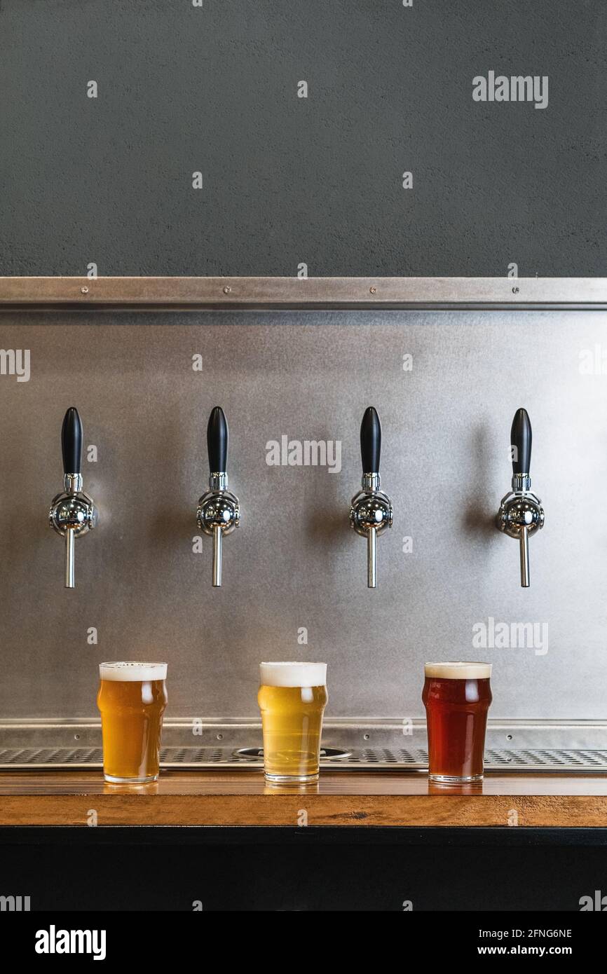 Different types of beer with foam in glass jugs against row of taps in ...