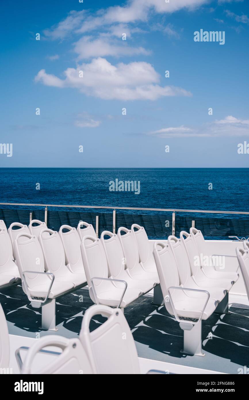 Empty white chairs on deck of cruise boat sailing in blue sea water ...