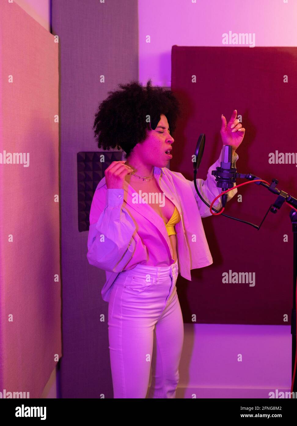 Black female singer performing song against microphone with pop filter ...