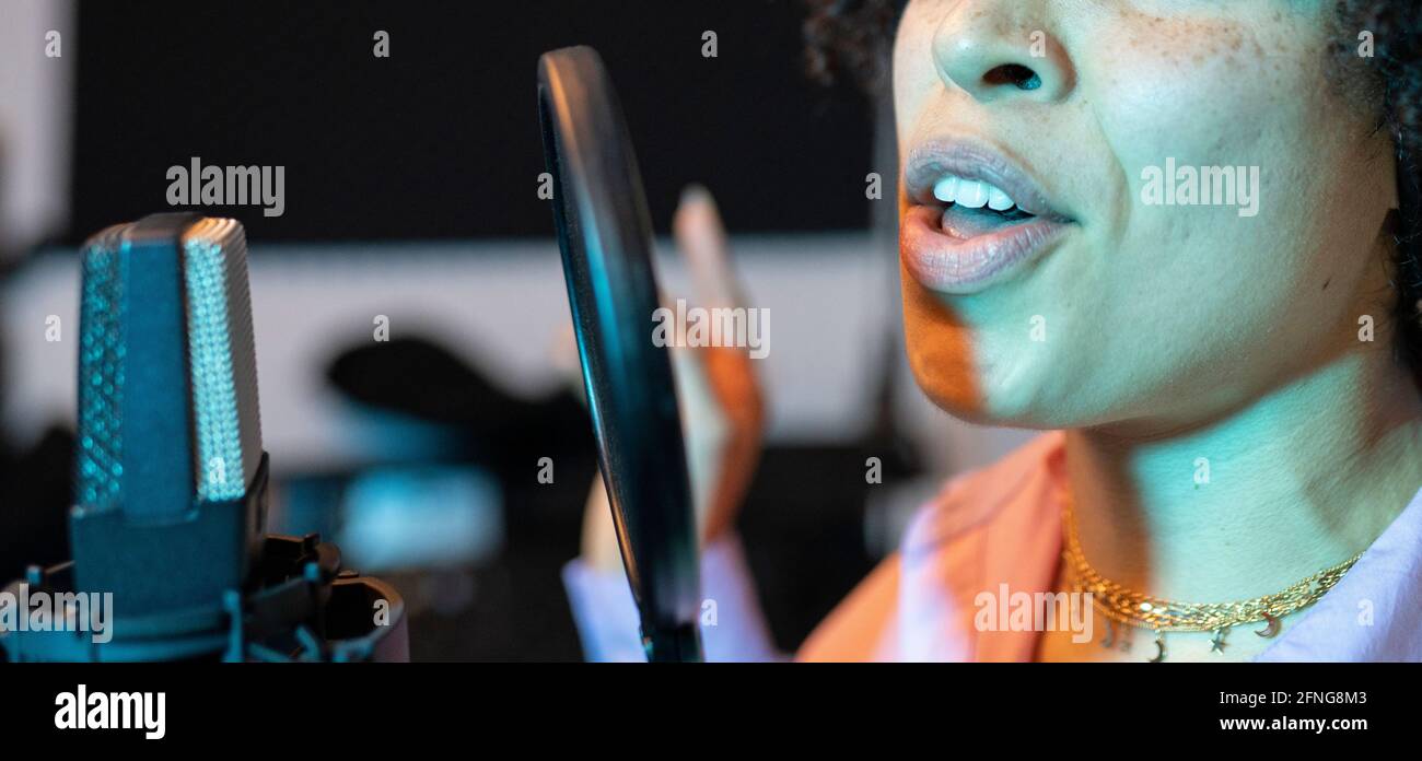 Black female singer performing song against microphone with pop filter ...