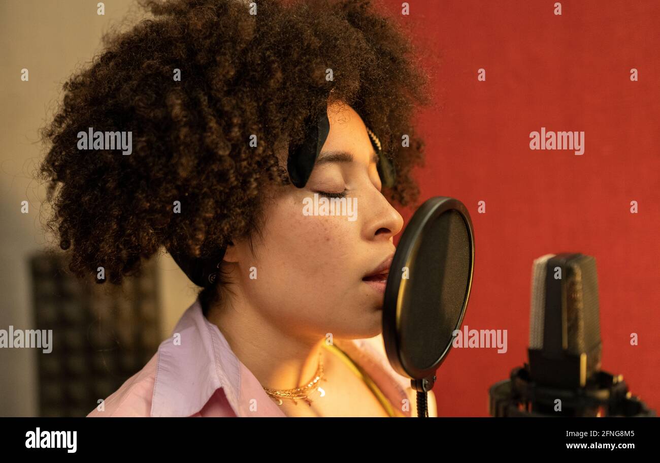 Black female singer performing song against microphone with pop filter ...