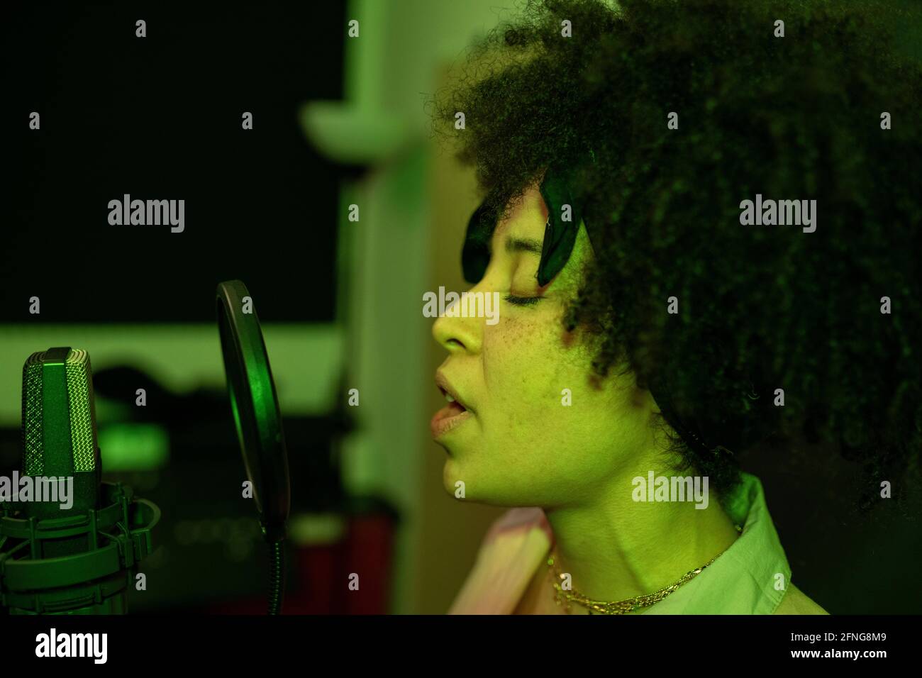 Black female singer performing song against microphone with pop filter ...