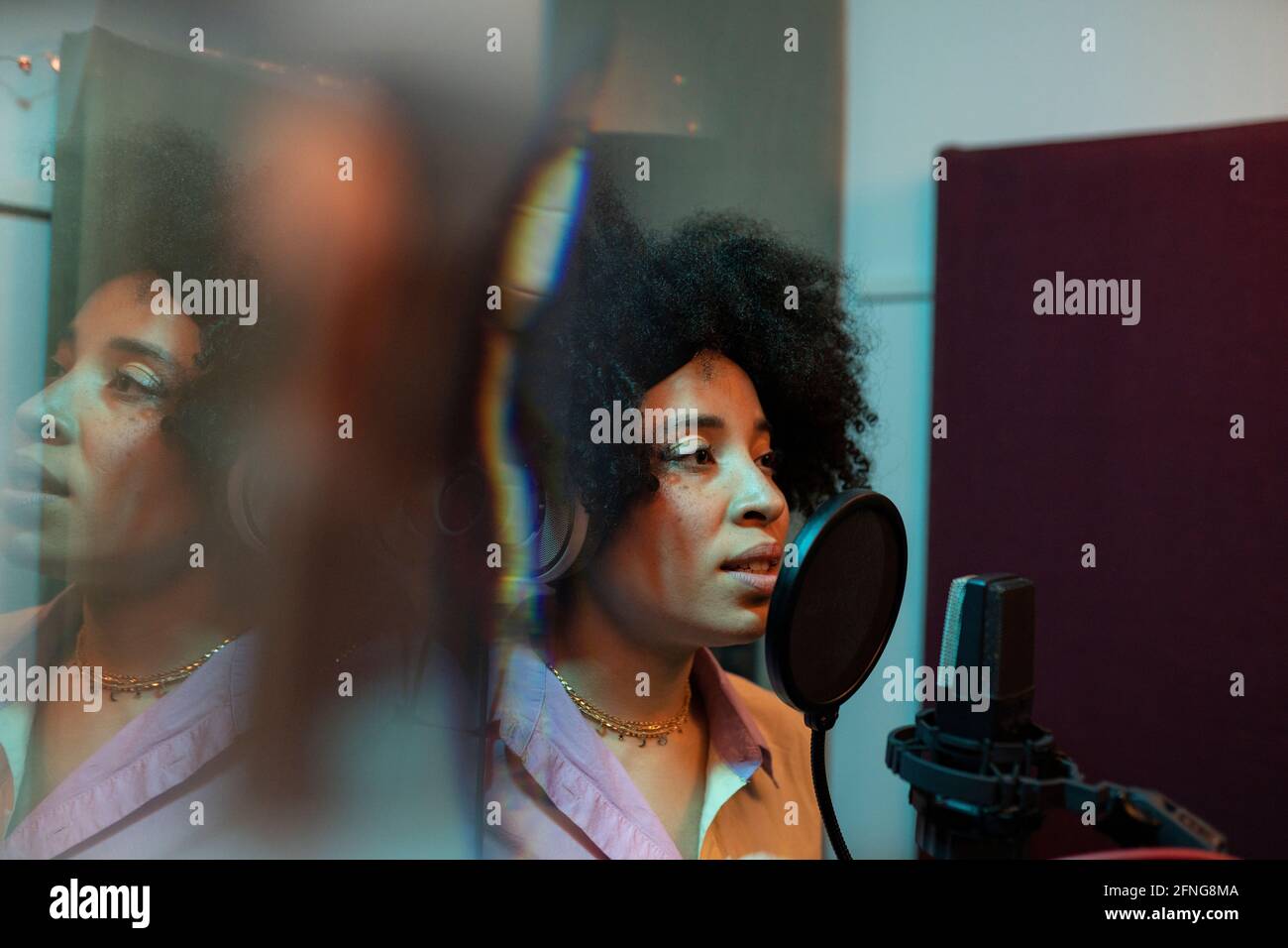 Black female singer performing song against microphone with pop filter ...