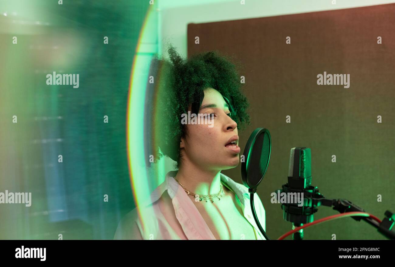 Black female singer performing song against microphone with pop filter ...