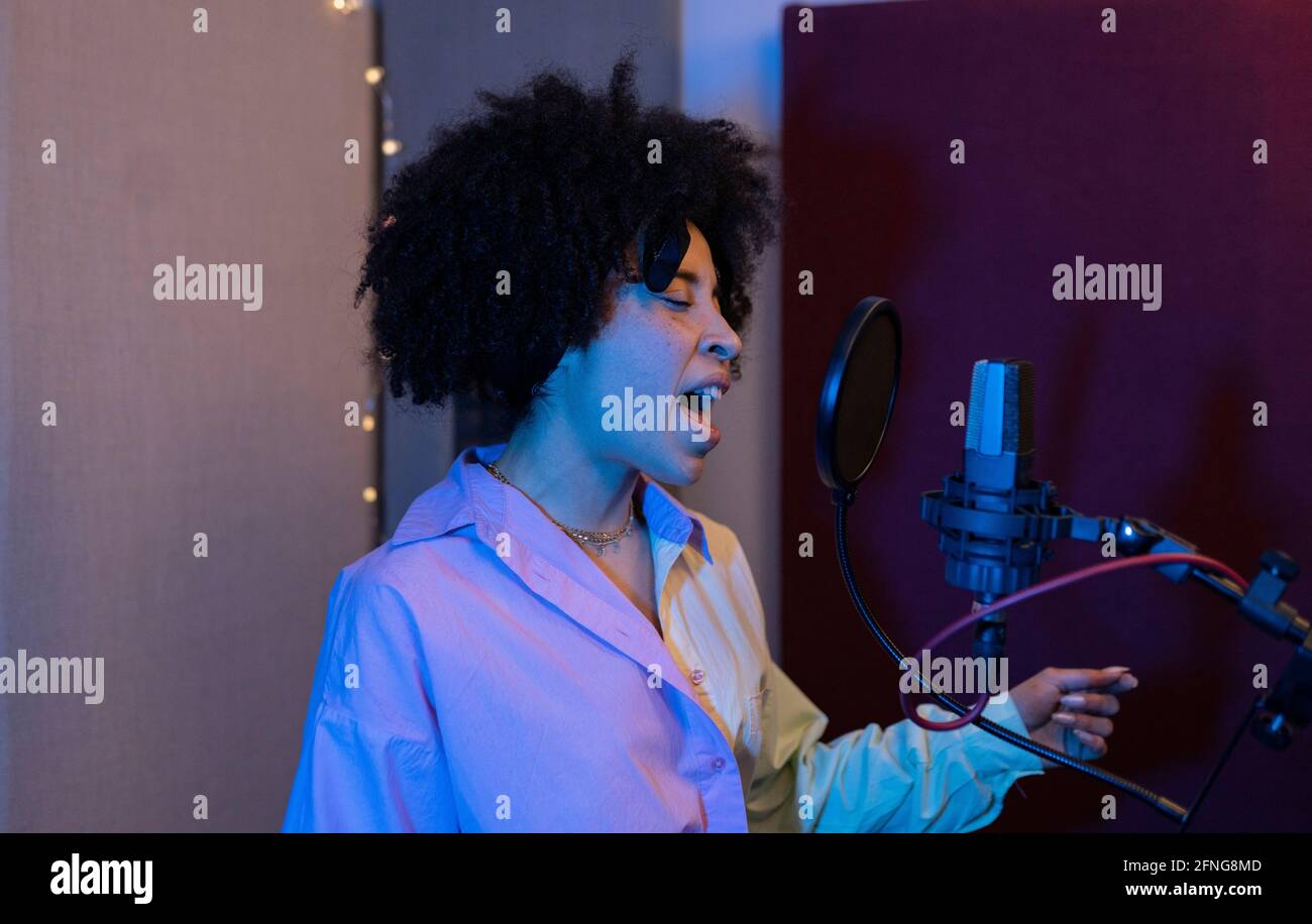 Black female singer performing song against microphone with pop filter ...