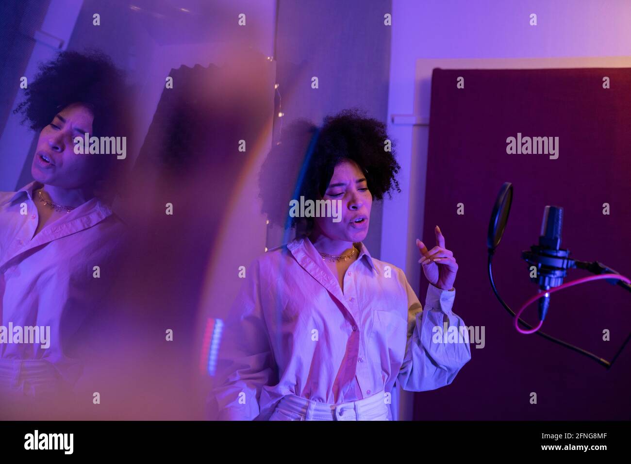 Black female singer performing song against microphone with pop filter ...