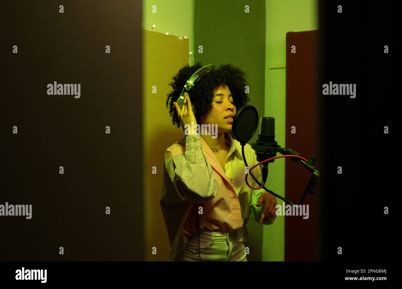 Black female singer performing song against microphone with pop filter ...